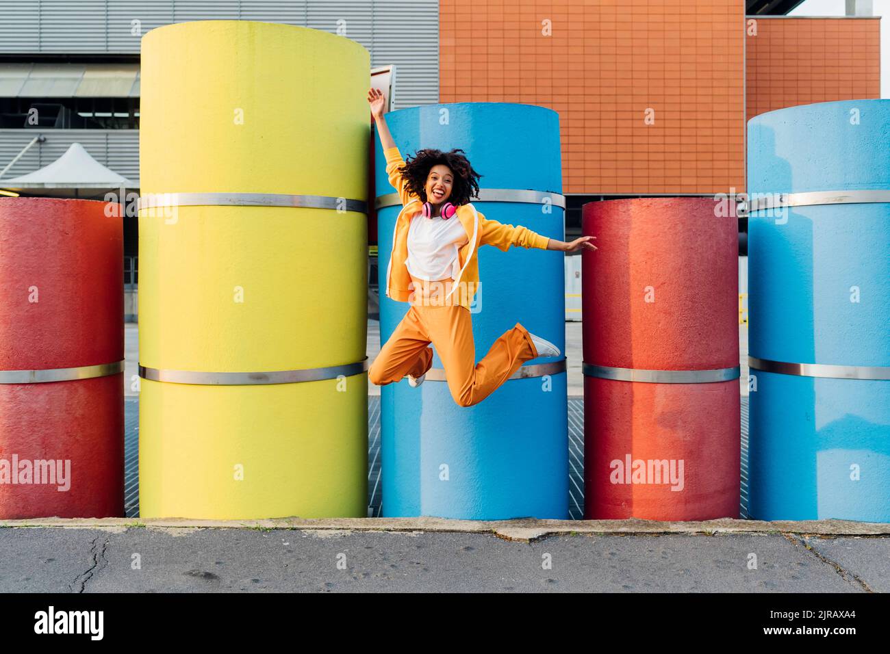 Happy woman jumping in front of colorful pipes Stock Photo - Alamy