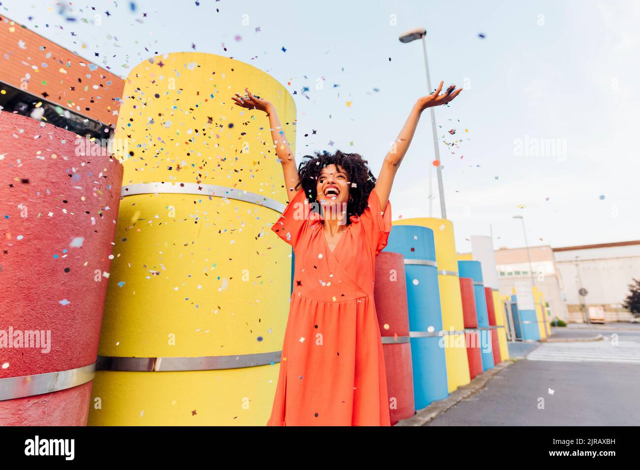 Playful woman throwing confetti by multi colored pipes Stock Photo - Alamy