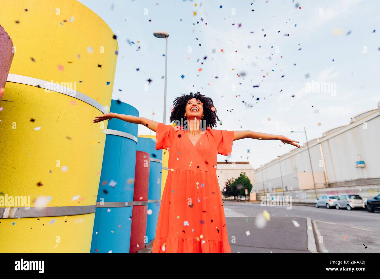 Happy woman throwing confetti by multi colored pipes Stock Photo - Alamy