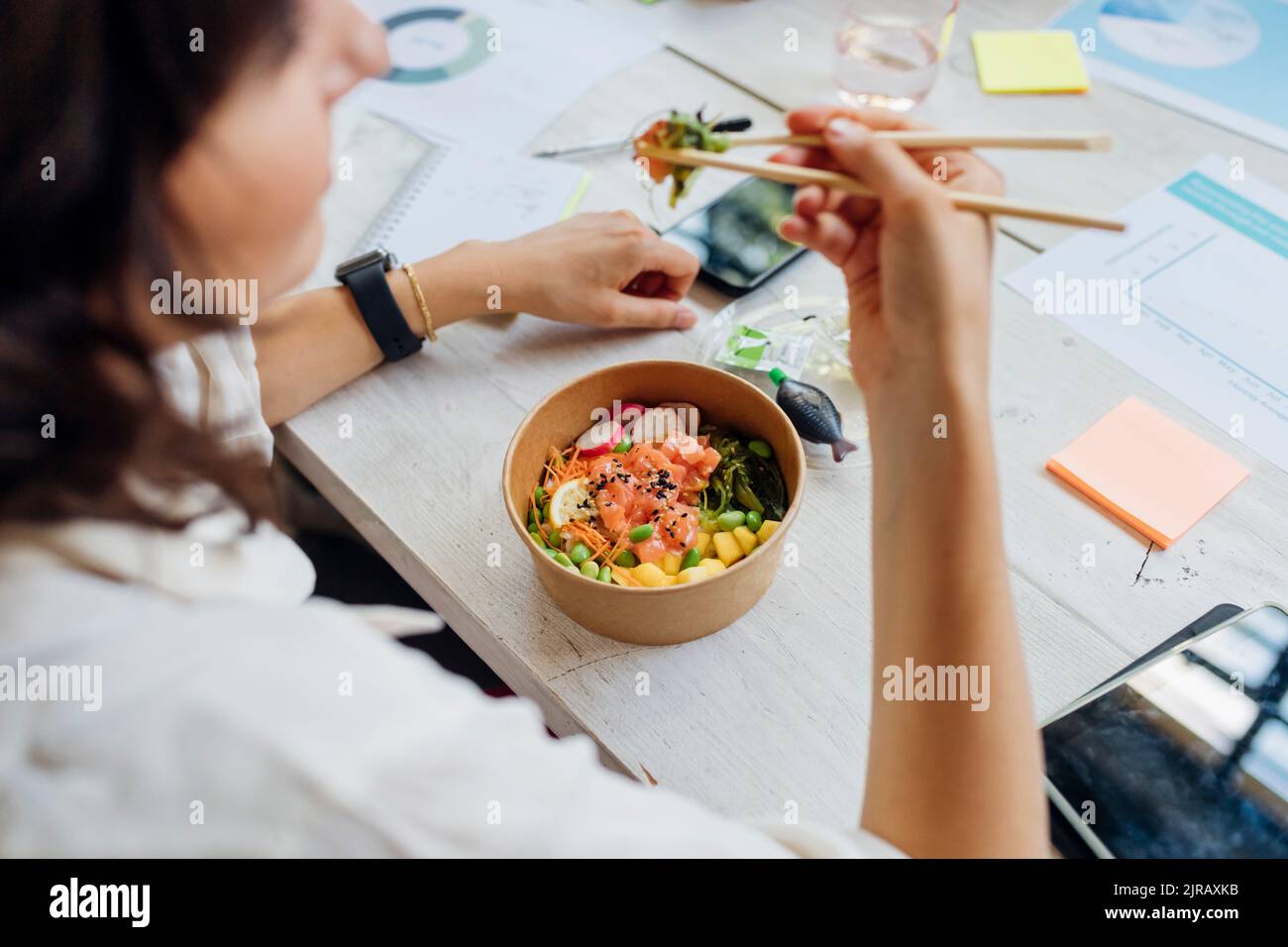 Businesswoman eating healthy poke bowl with chopsticks in lunch break ...