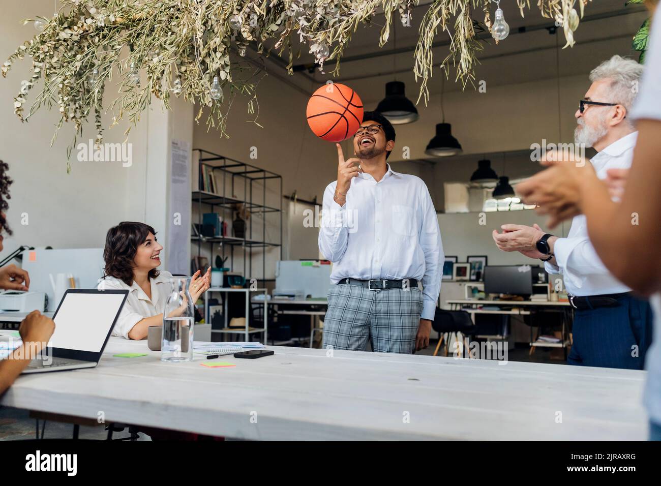 Playful businessman spinning basketball on finger by colleagues ...
