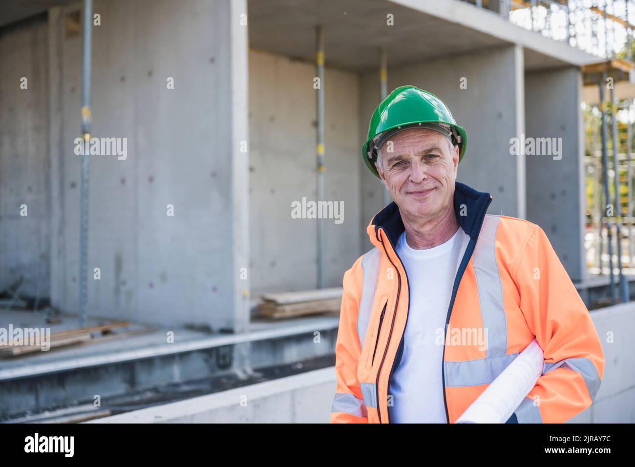 Smiling building contractor with blueprint standing at construction ...