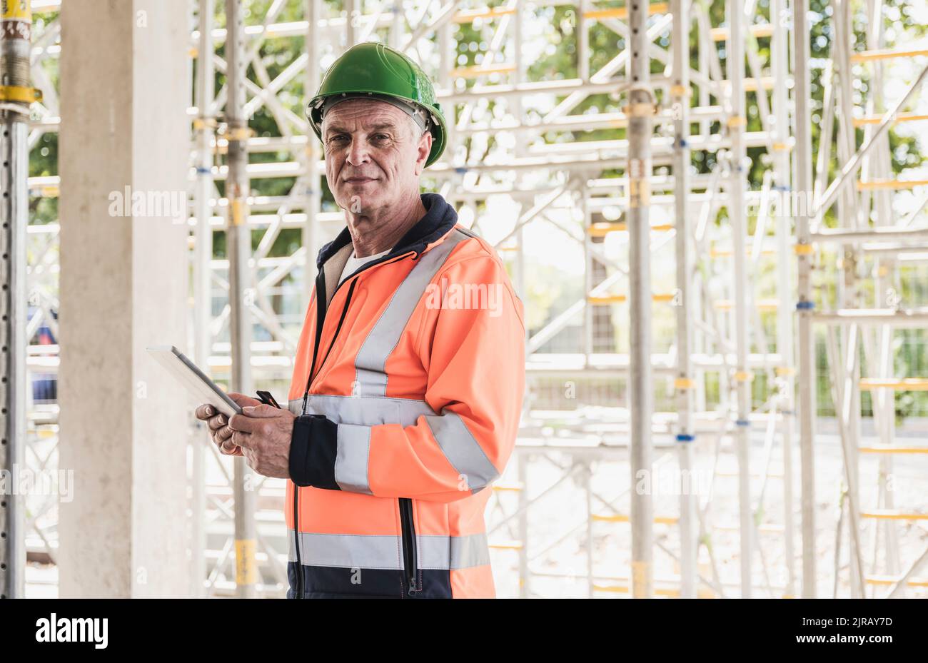 Senior contractor holding tablet PC standing in front of scaffolding ...