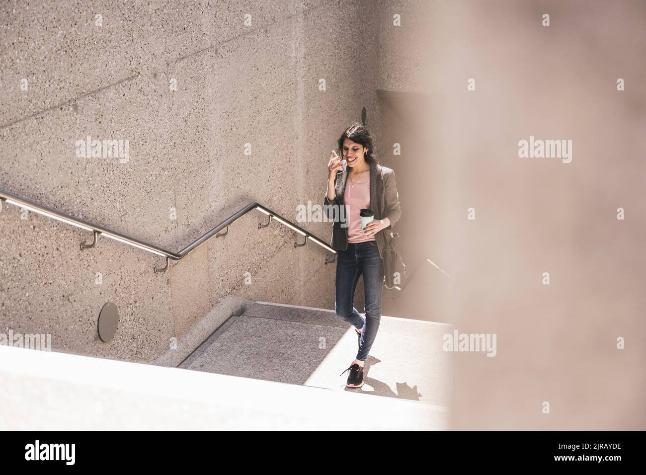 Smiling transgender woman talking on phone climbing steps of subway ...
