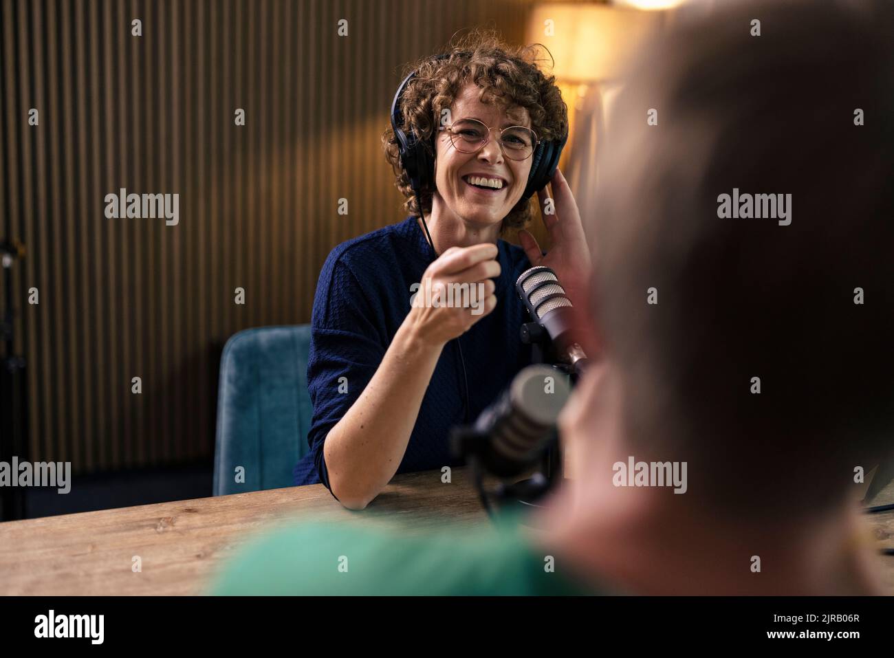 Happy presenter wearing eyeglasses talking with guest in radio station ...