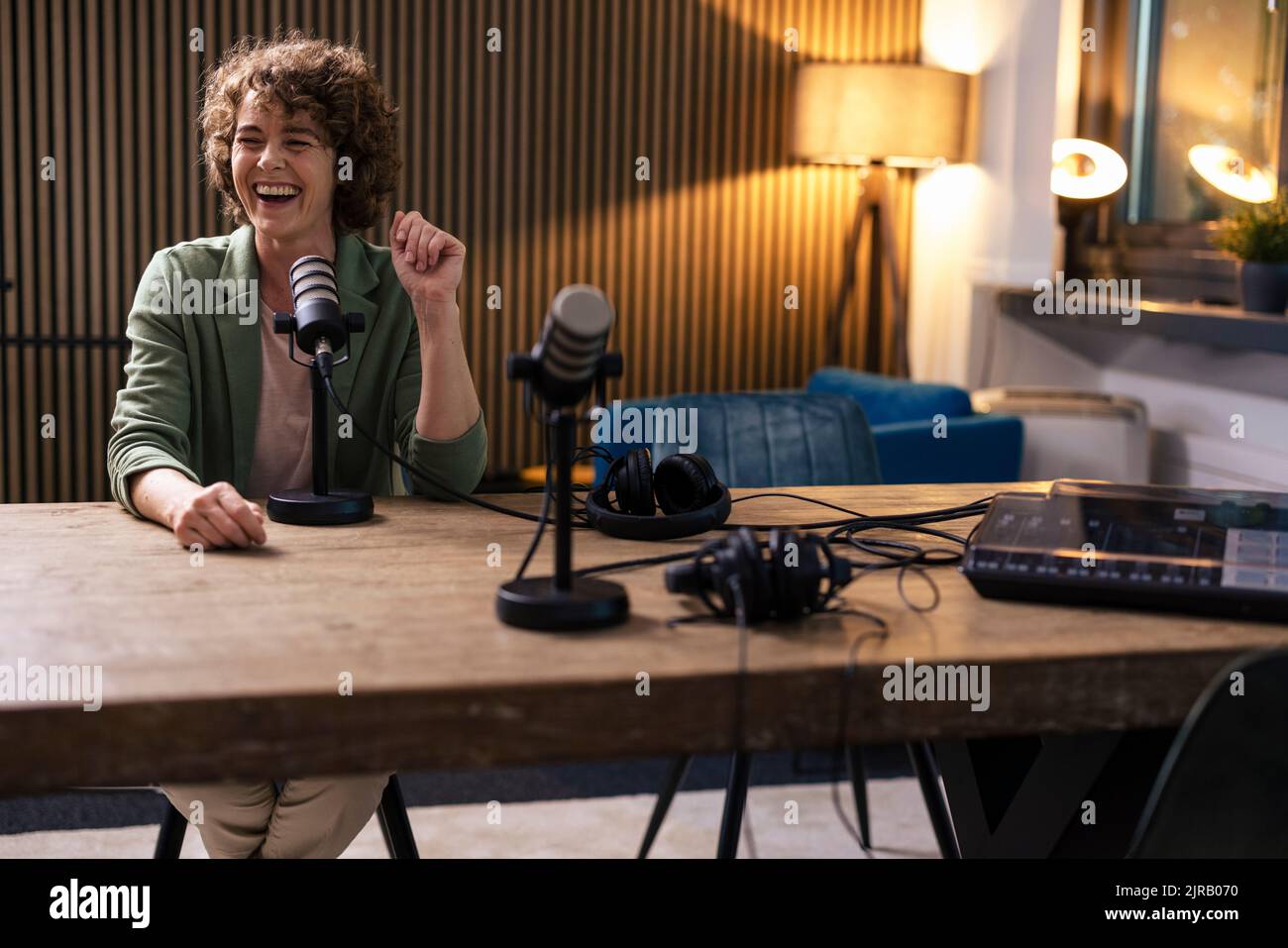 Cheerful presenter with microphone sitting at desk in recording studio ...