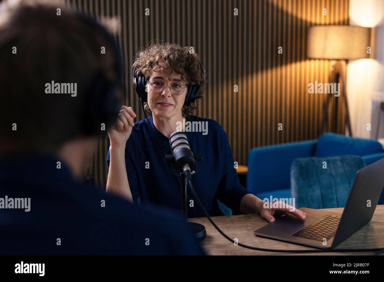 Radio DJ wearing eyeglasses and headset interviewing guest in recording ...