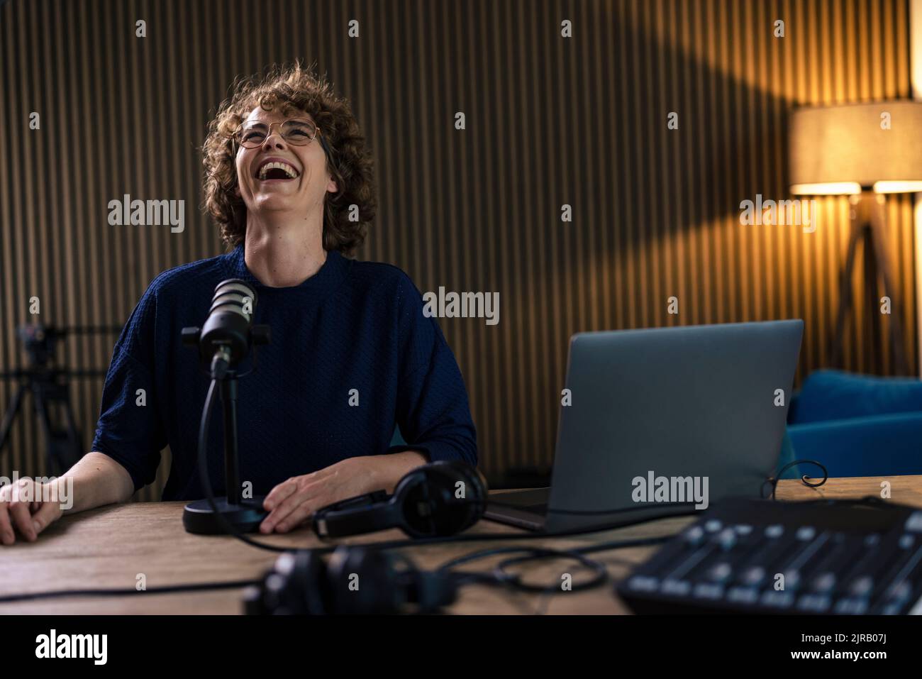Cheerful presenter with microphone and laptop sitting at desk in radio ...