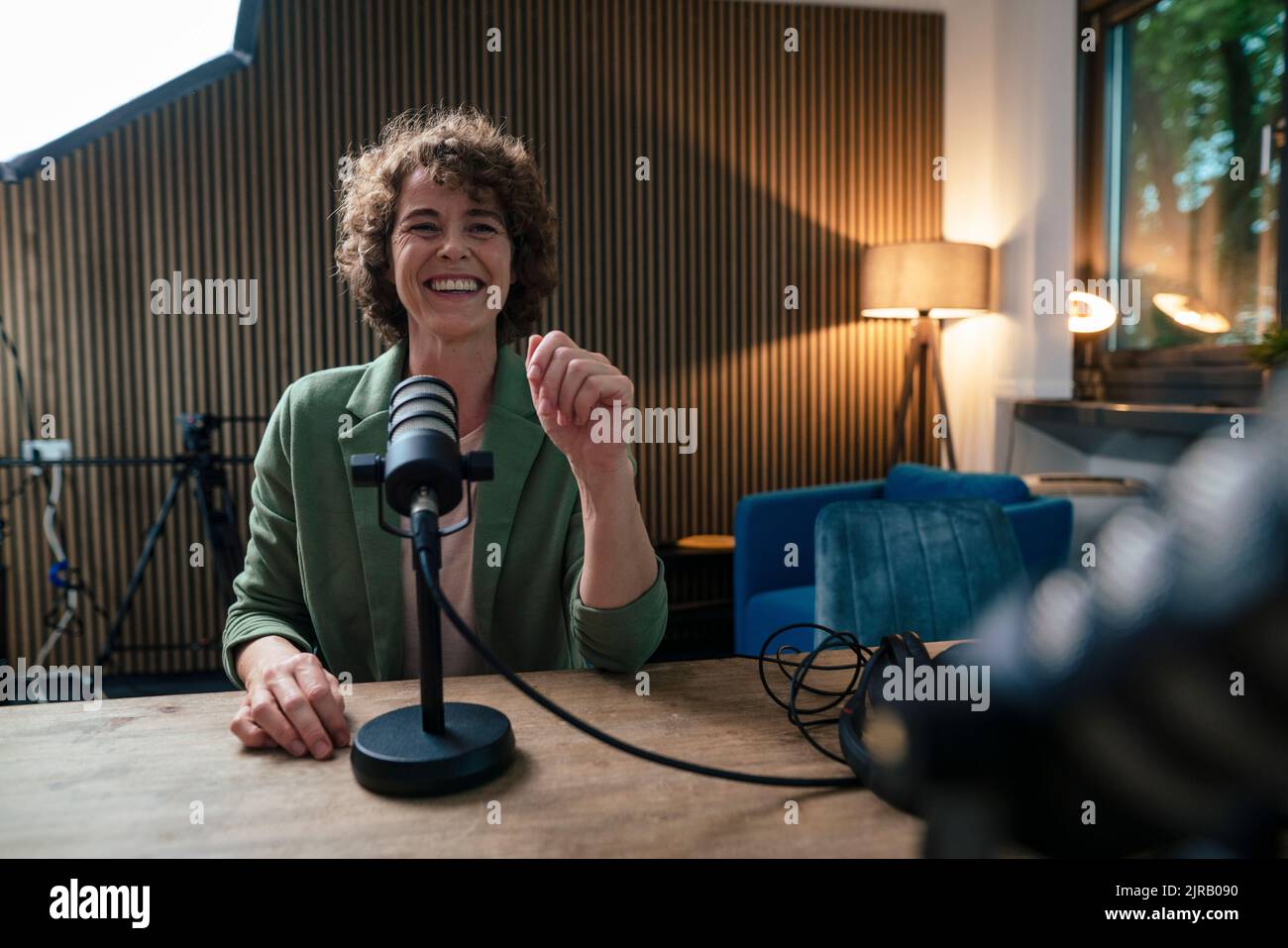 Happy presenter sitting with microphone at desk in recording studio ...