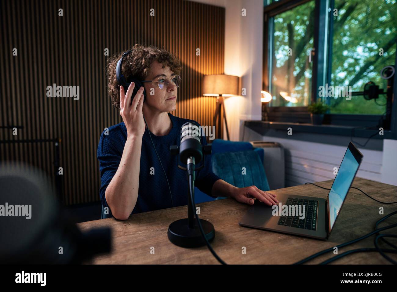 Radio DJ sitting with microphone and laptop at desk in recording studio ...