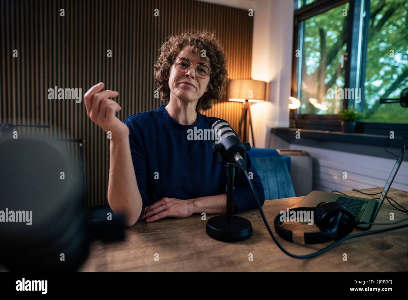 Presenter wearing eyeglasses sitting with microphone at desk in ...