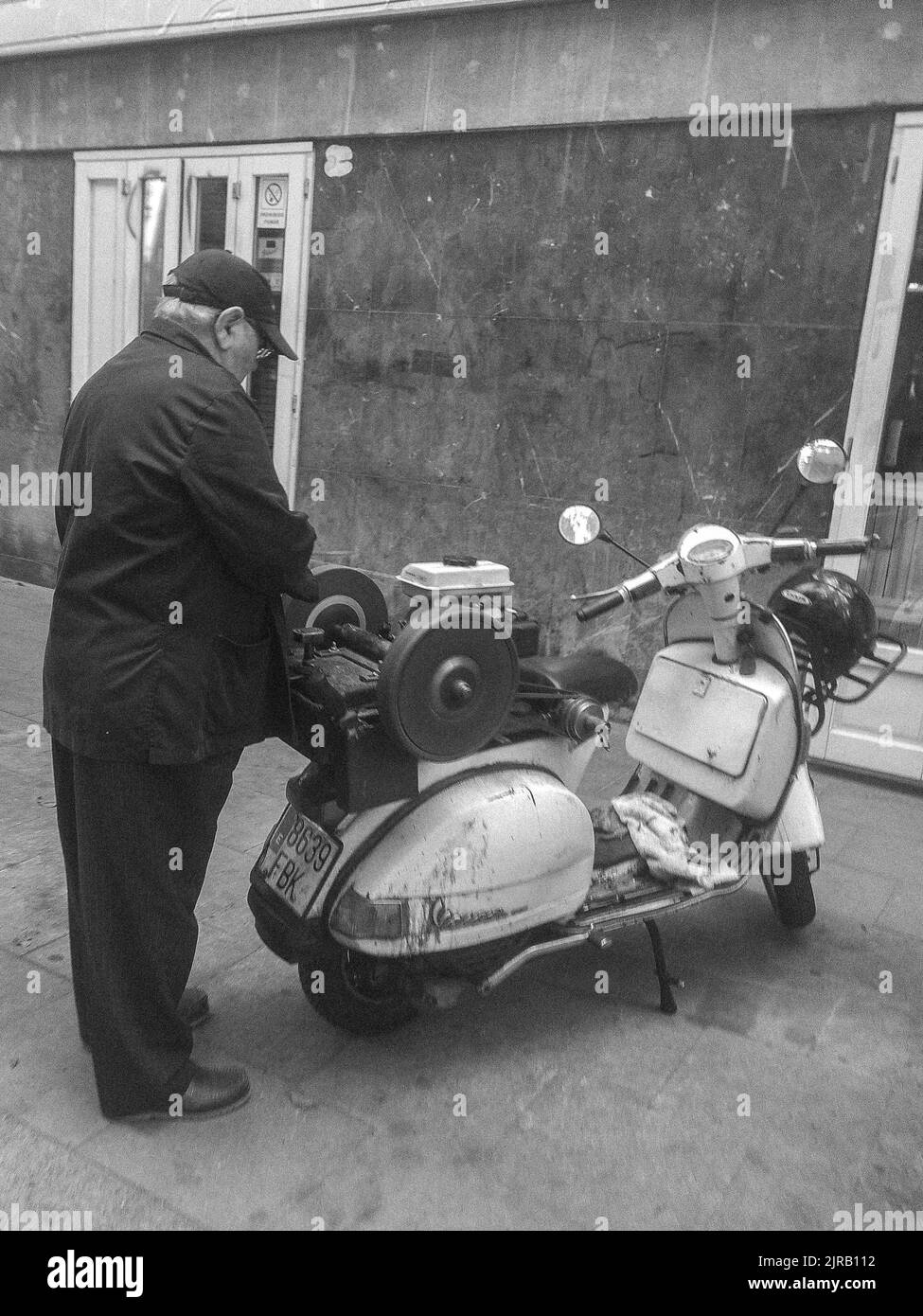 A vertical grayscale shot of a man standing behind Italian Vespa ...
