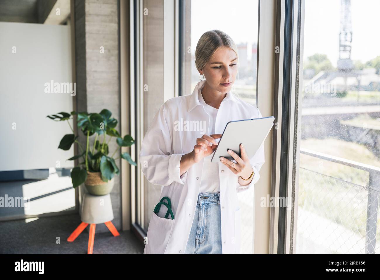 Doctor wearing lab coat using tablet PC standing near window Stock ...