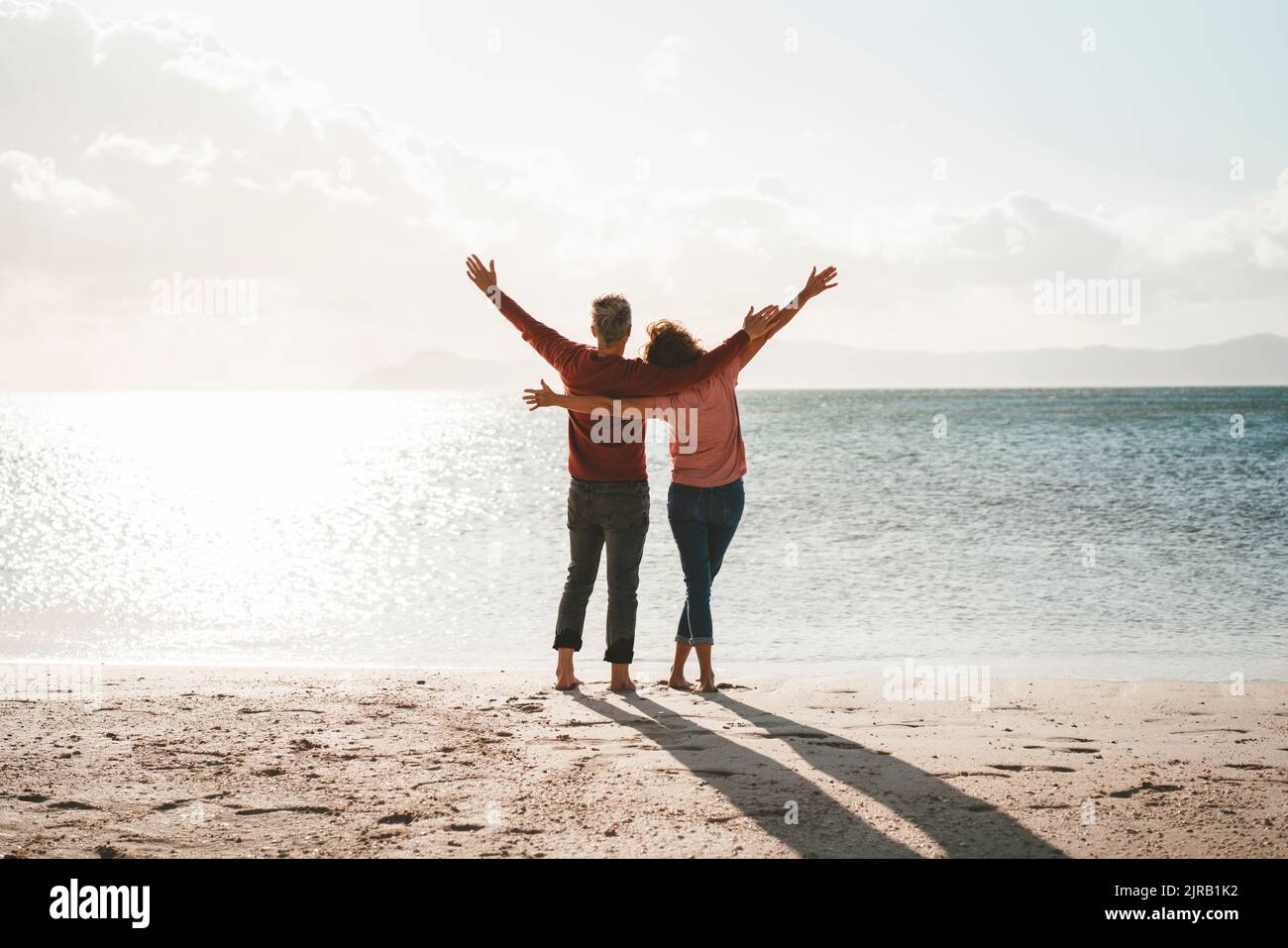 Carefree couple with arms outstretched standing on shore at beach Stock ...