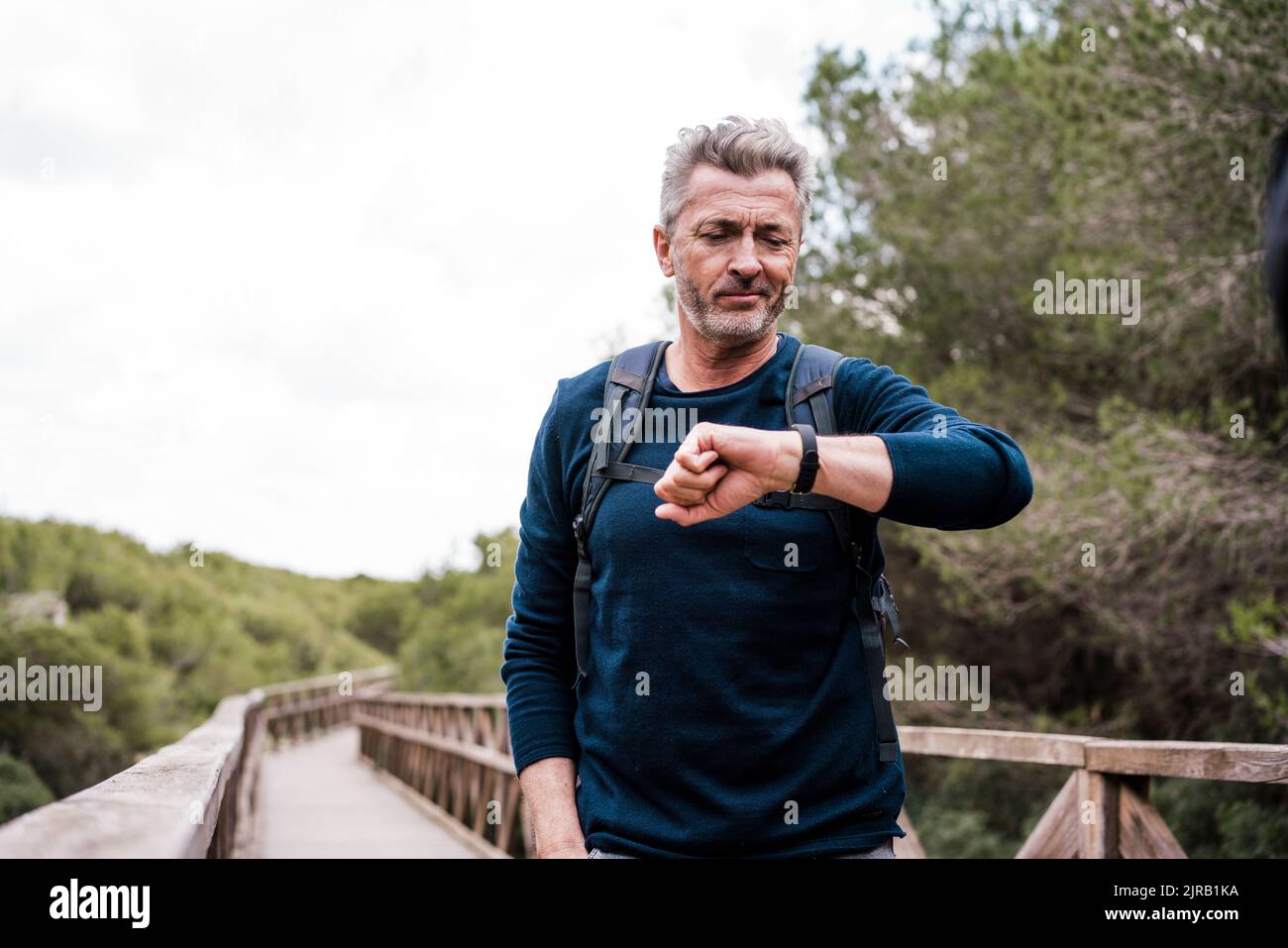Mature man checking time on wristwatch standing at footbridge Stock ...