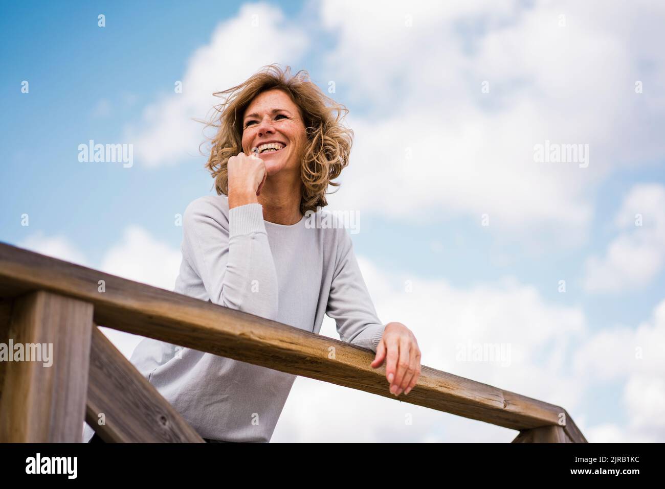 Happy mature woman leaning on railing under cloudy sky Stock Photo - Alamy
