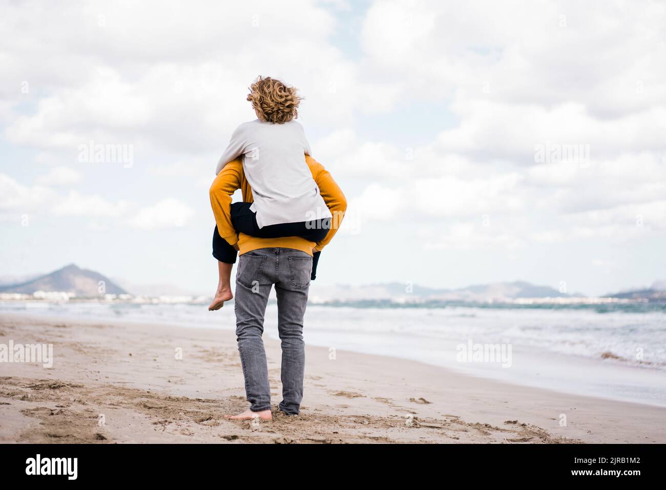 Man giving piggyback ride to woman on shore at beach Stock Photo - Alamy