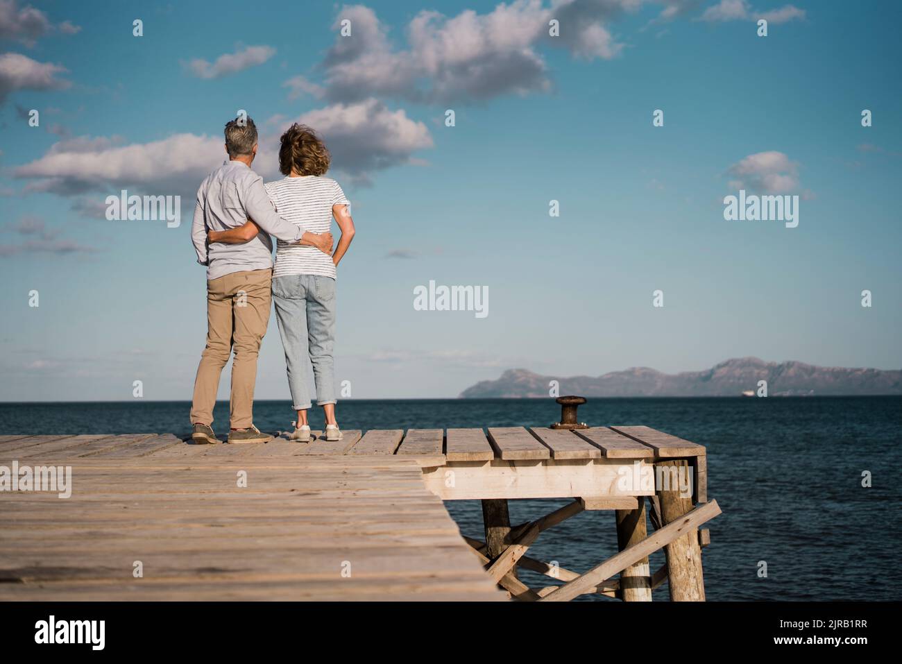 Loving mature couple with arms around each other standing on jetty ...