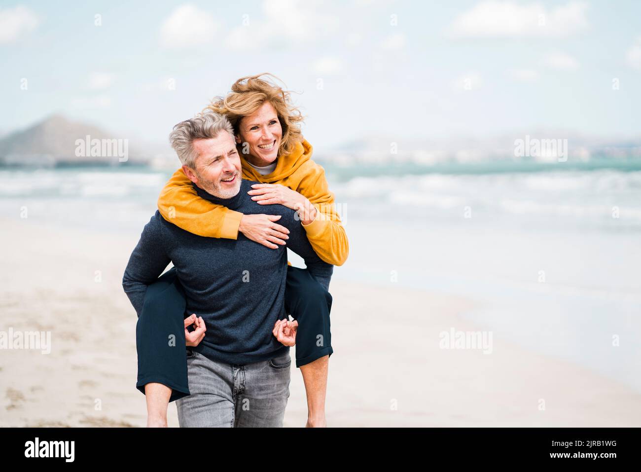 Happy man giving piggyback ride to woman on shore at beach Stock Photo ...