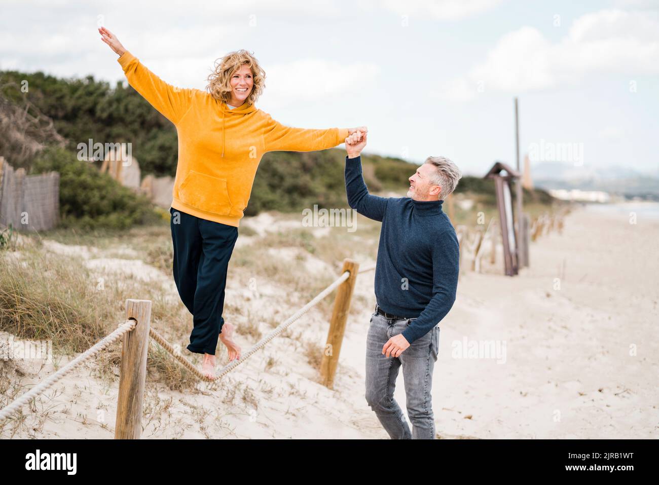 Carefree woman walking on rope with support of man at beach Stock Photo ...
