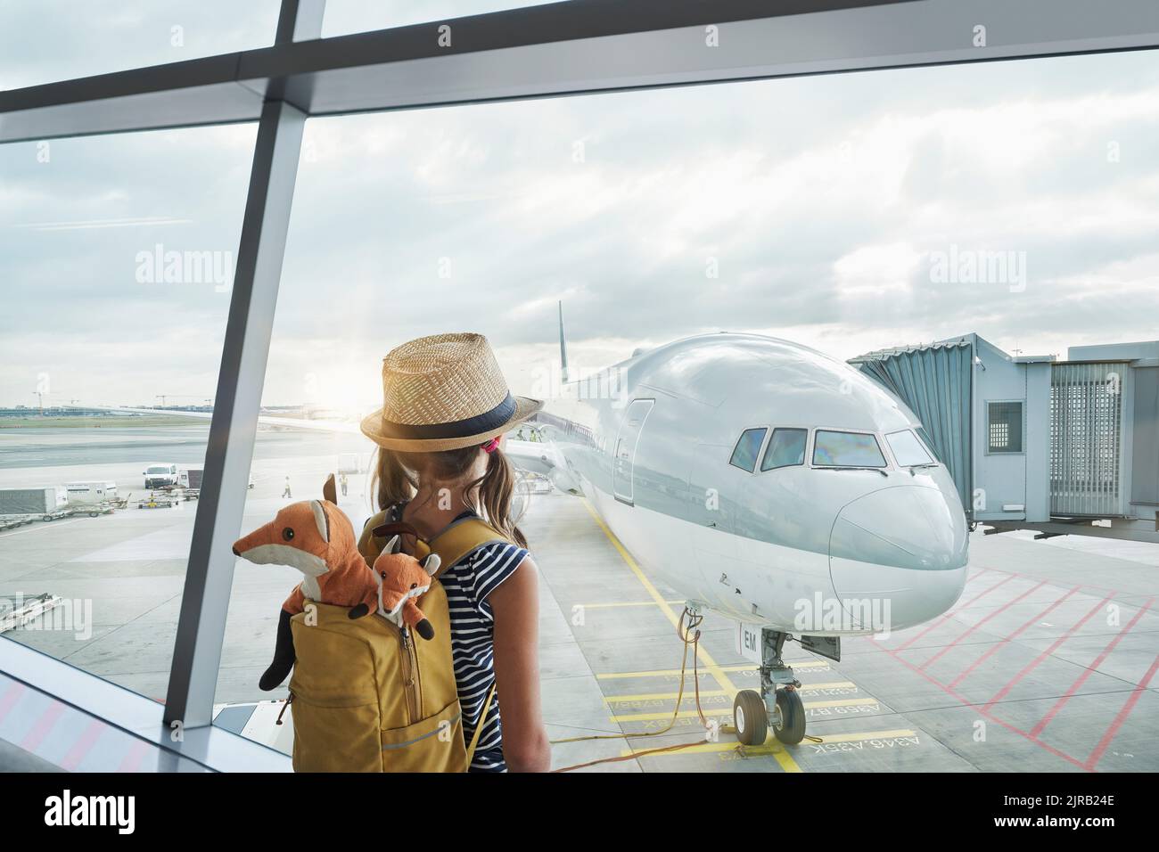 Girl with backpack watching airplane through glass window Stock Photo ...