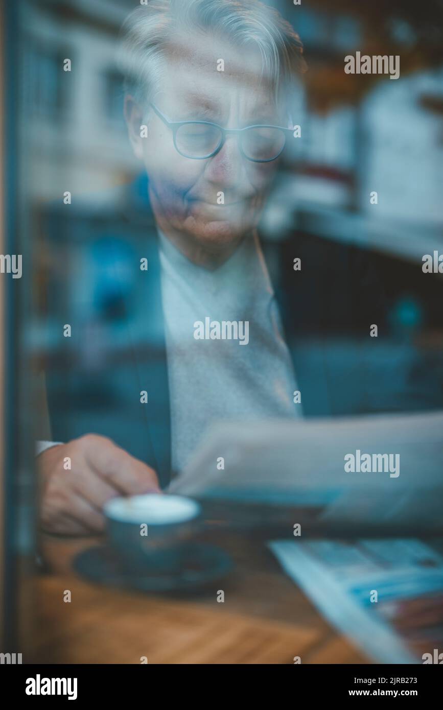 Businessman reading newspaper seen through window of cafe Stock Photo ...