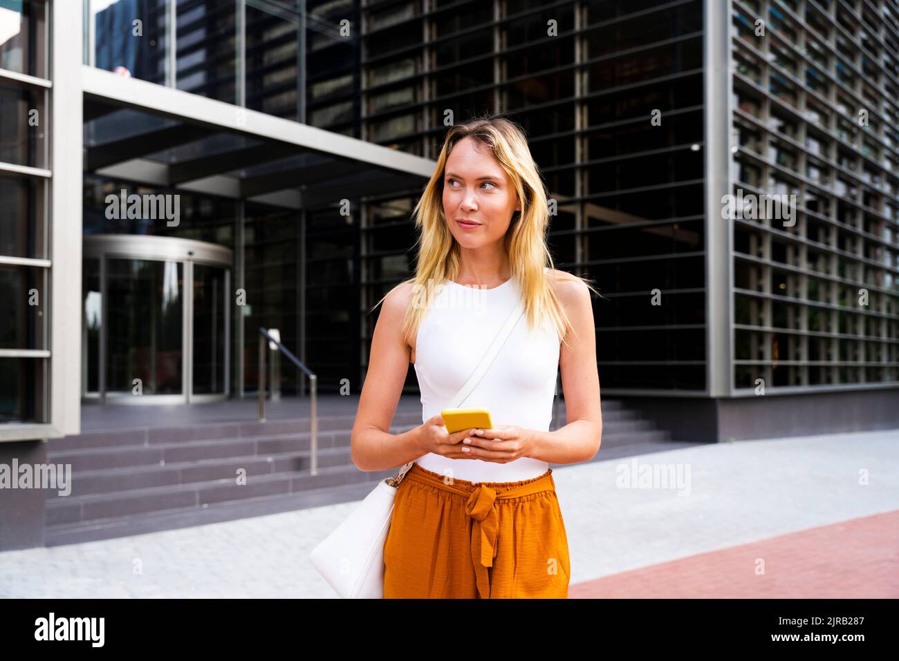 Contemplative woman with smart phone outside shopping mall Stock Photo ...