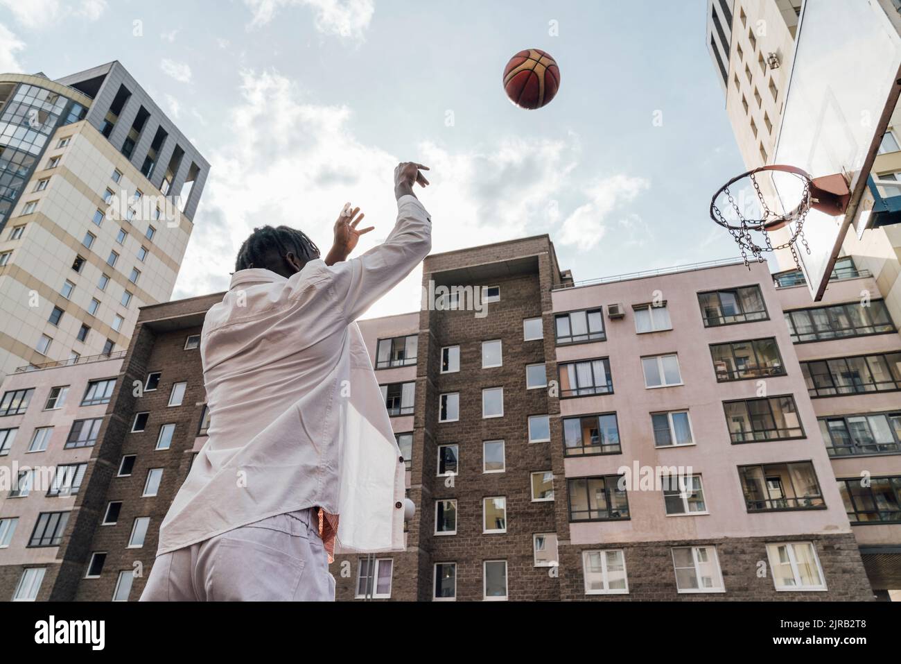 Man throwing basketball in hoop in front of buildings Stock Photo - Alamy