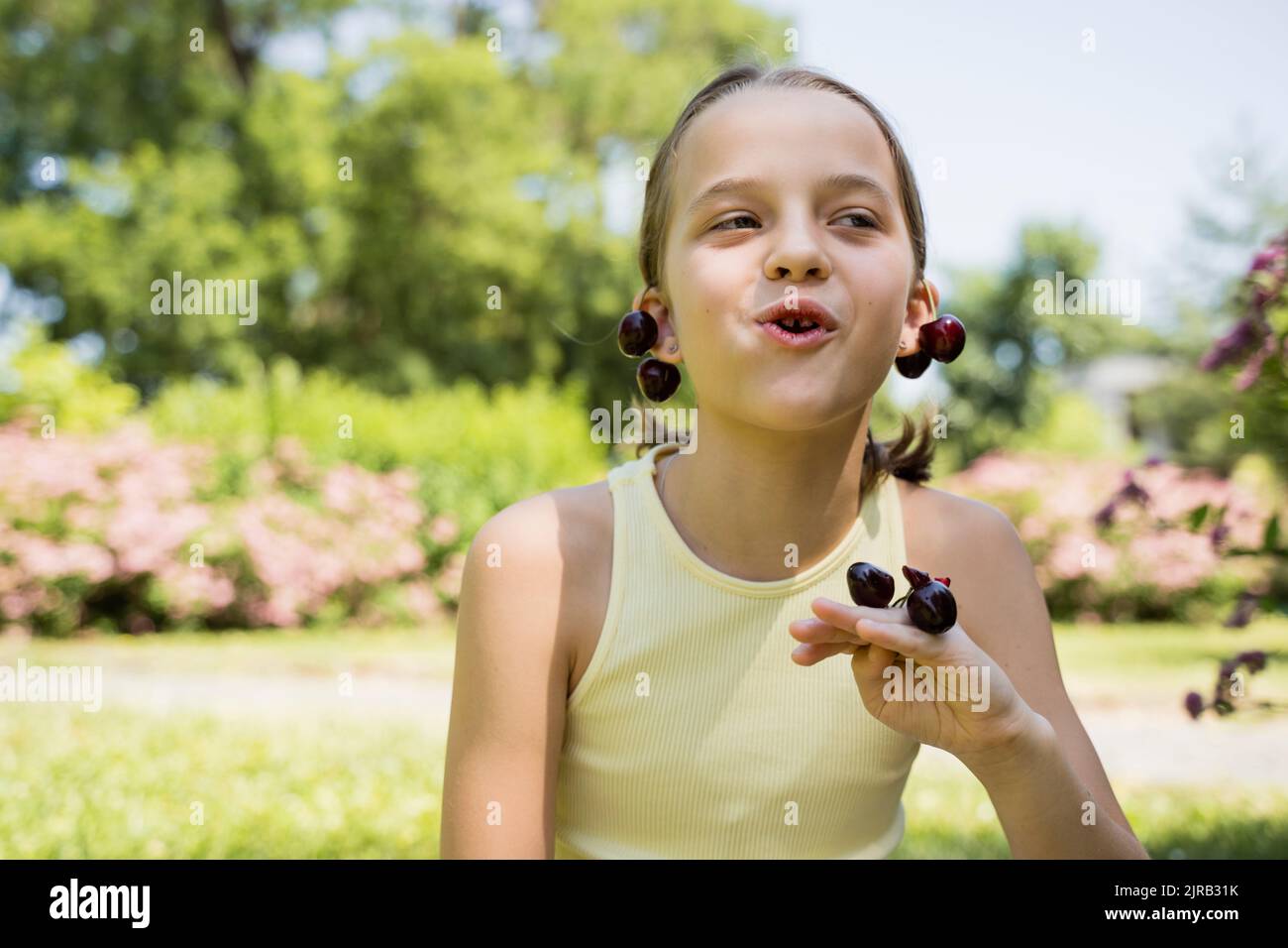 Cute girl eating cherries at park Stock Photo - Alamy