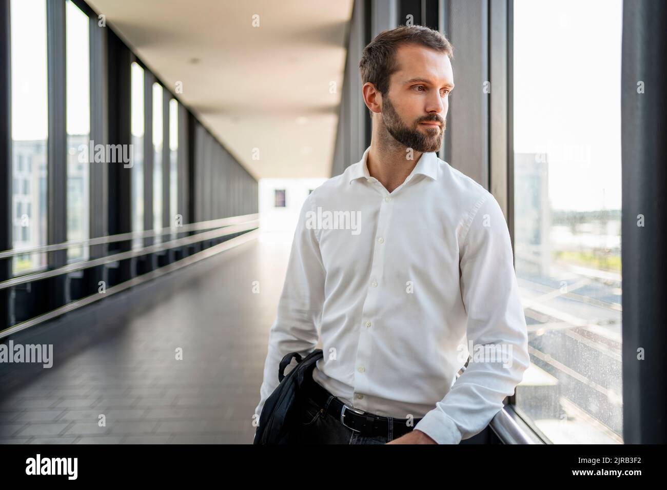 Contemplative young businessman looking through window at elevated ...