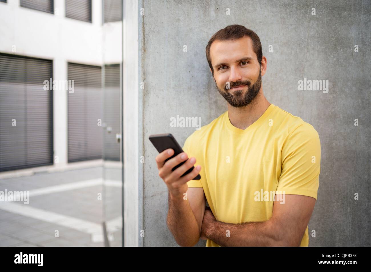 Smiling young man holding mobile phone standing in front of wall Stock ...