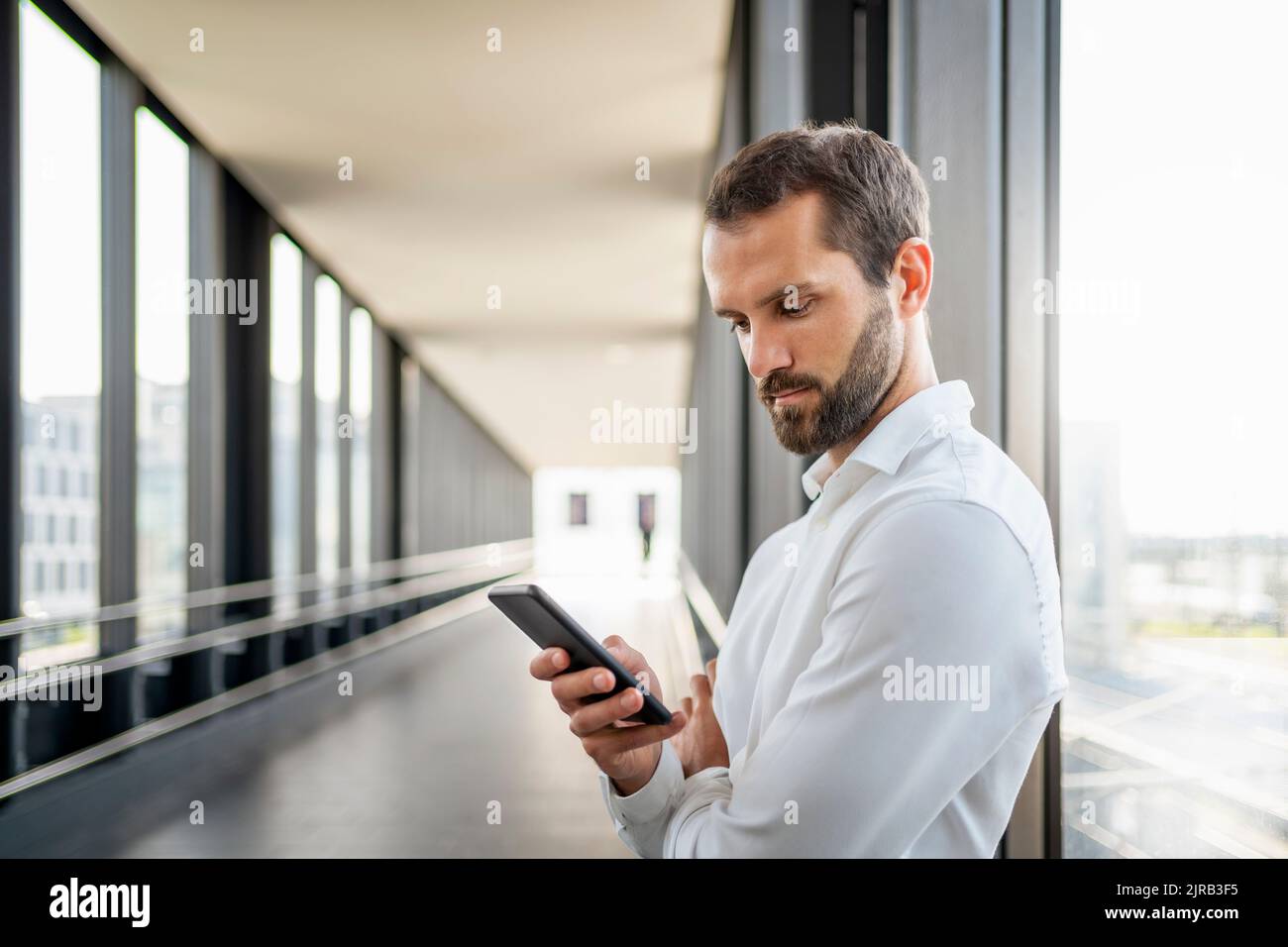 Young businessman using smart phone standing by window on elevated ...