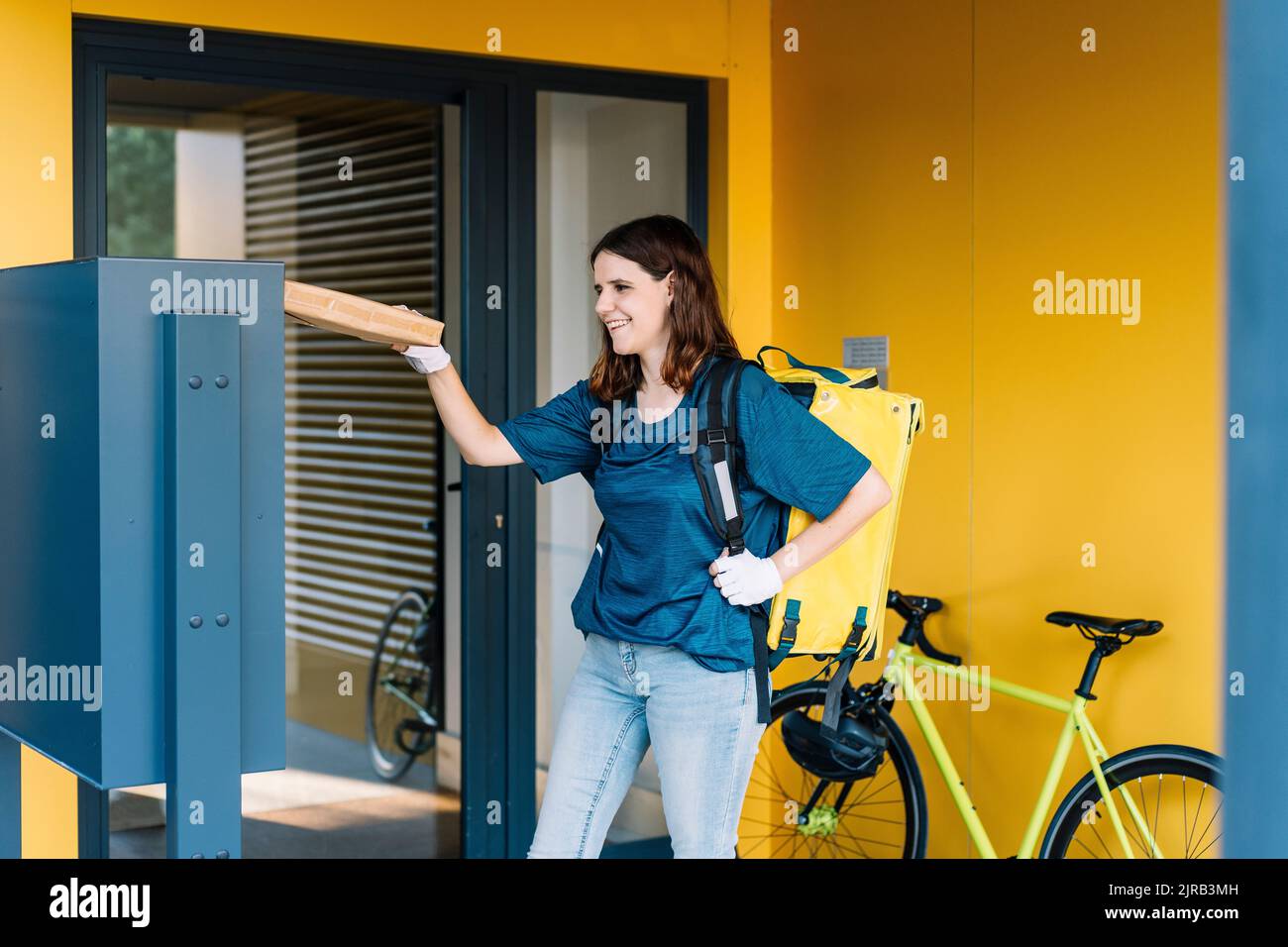 Smiling delivery woman keeping package in mailbox Stock Photo - Alamy