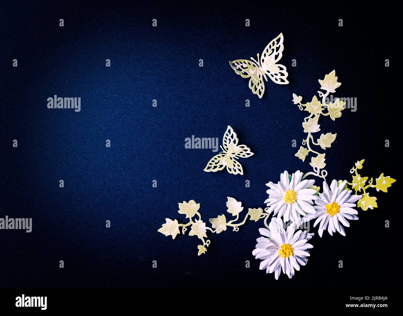 A composition of hand-made paper daisies and butterflies on a dark blue ...
