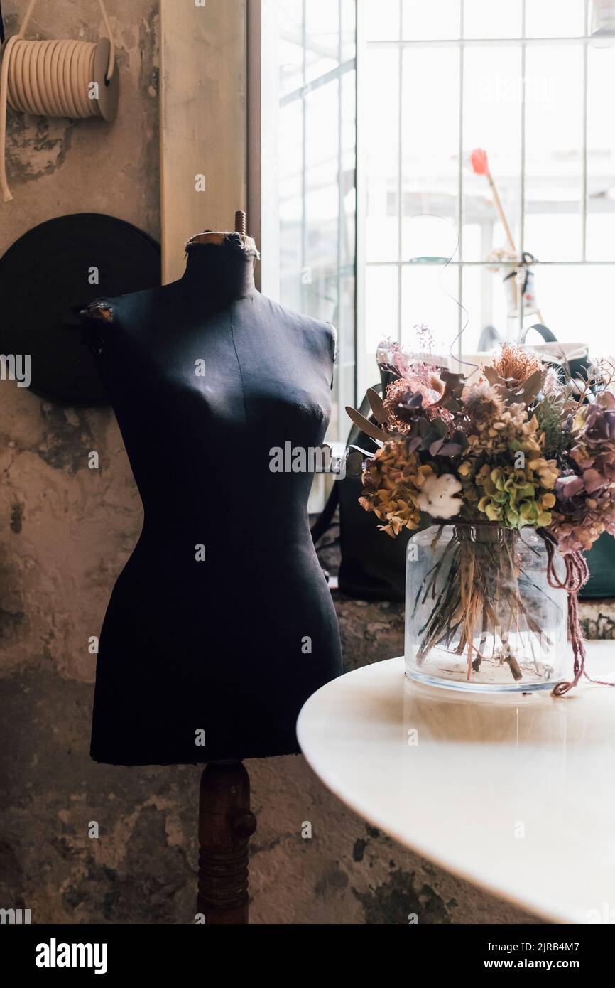 Dressmaker's mannequin by flower vase on table at workshop Stock Photo ...
