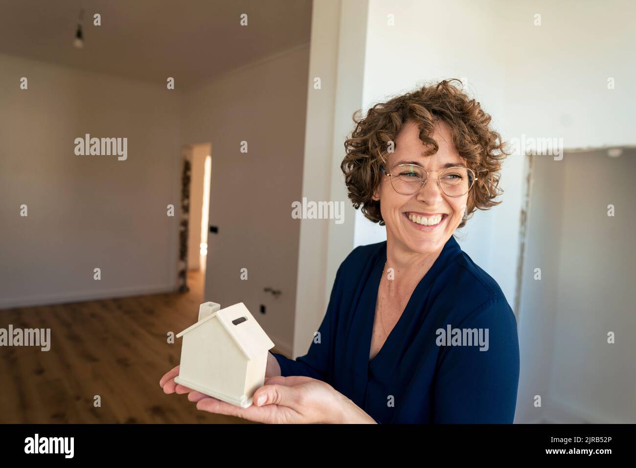 Happy real estate agent with curly hair holding model house Stock Photo ...