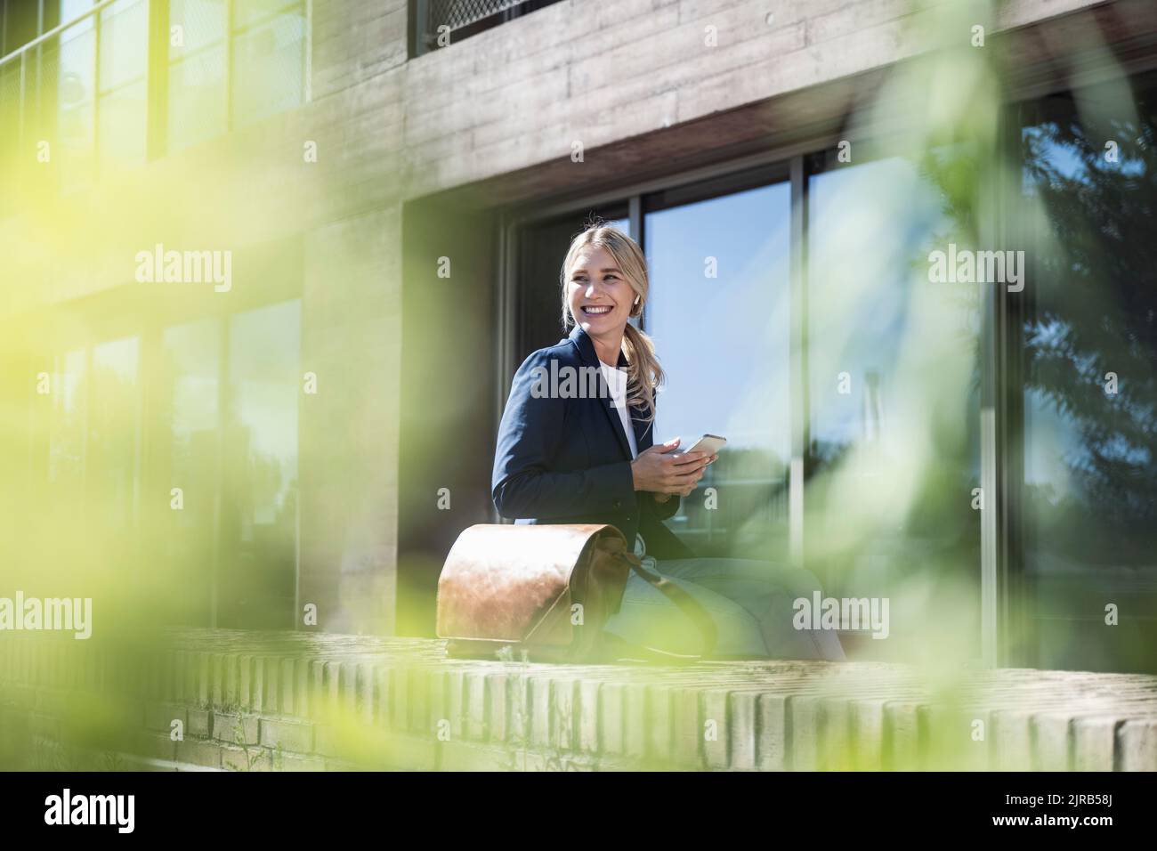Happy young woman with smart phone sitting on wall Stock Photo - Alamy