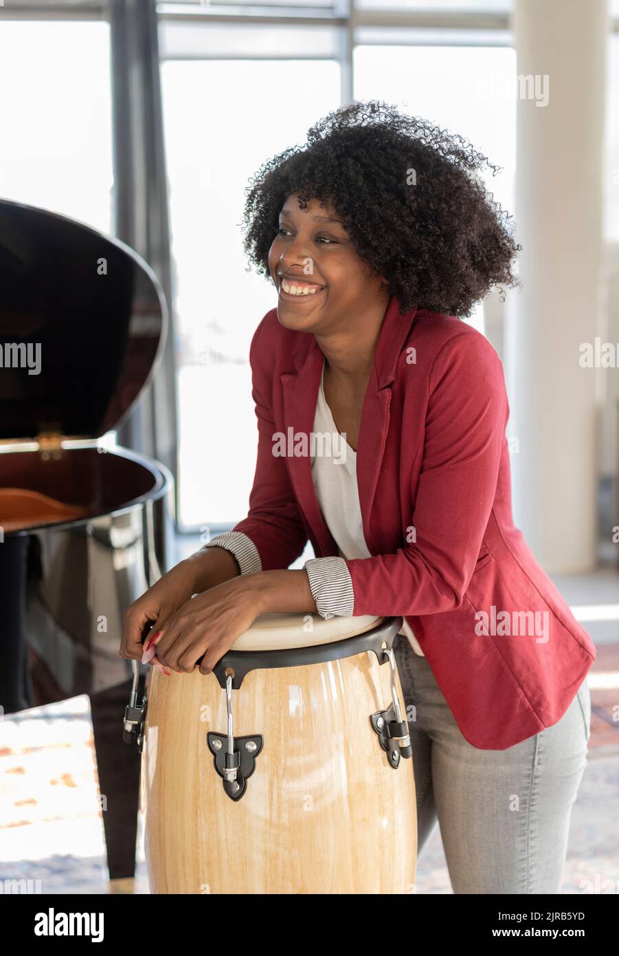 Happy businesswoman with Afro hairstyle leaning on conga drum in office ...