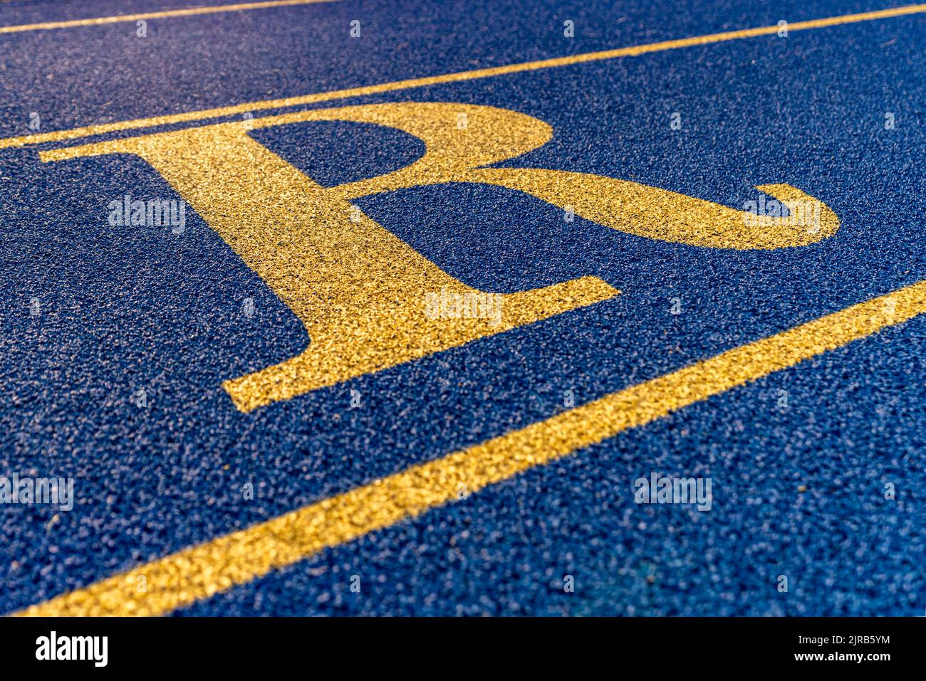 Close up the letter, initial R on a new blue running track with yellow ...