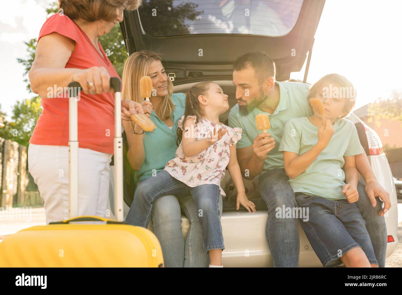 Smiling family eating ice pops sitting in car trunk Stock Photo - Alamy