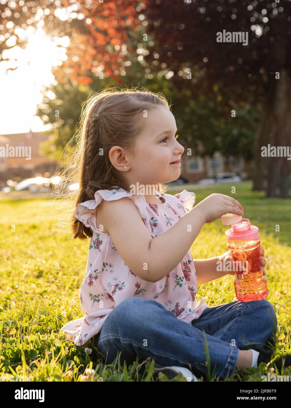 Cute girl dipping bubble wand in bottle at park Stock Photo - Alamy