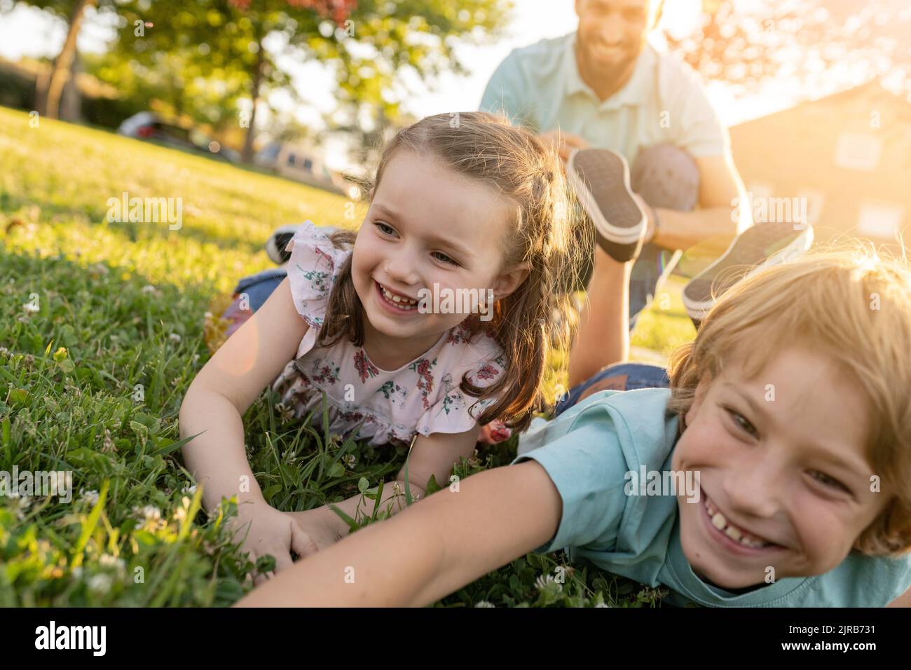 Happy siblings with father lying at park Stock Photo - Alamy