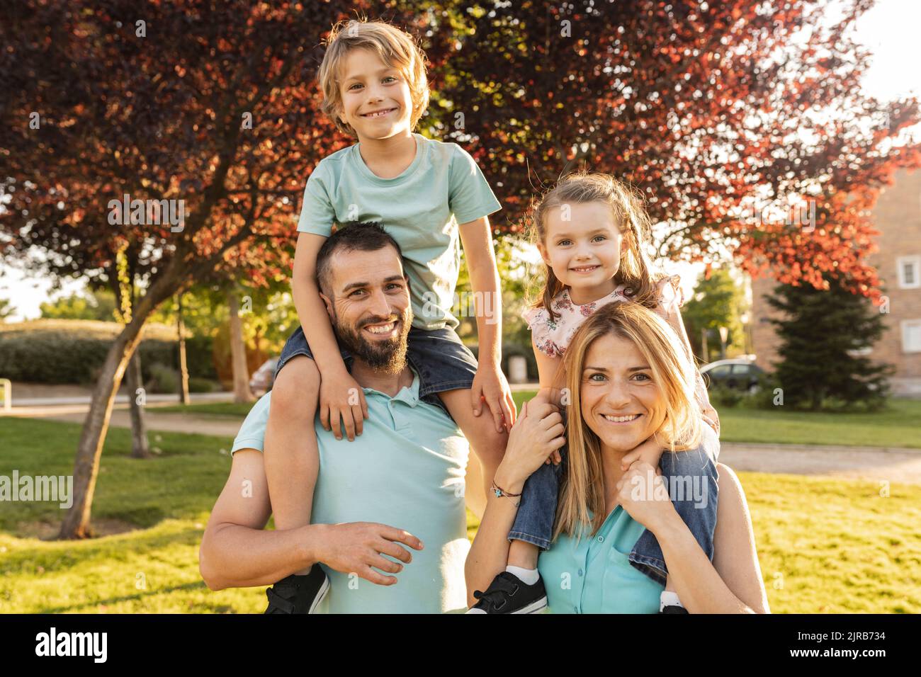 Parents carrying son and daughter on shoulders at park Stock Photo - Alamy