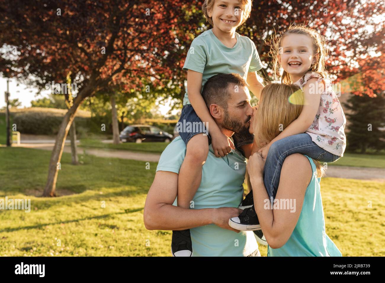 Parents carrying children on shoulders and kissing each other Stock ...