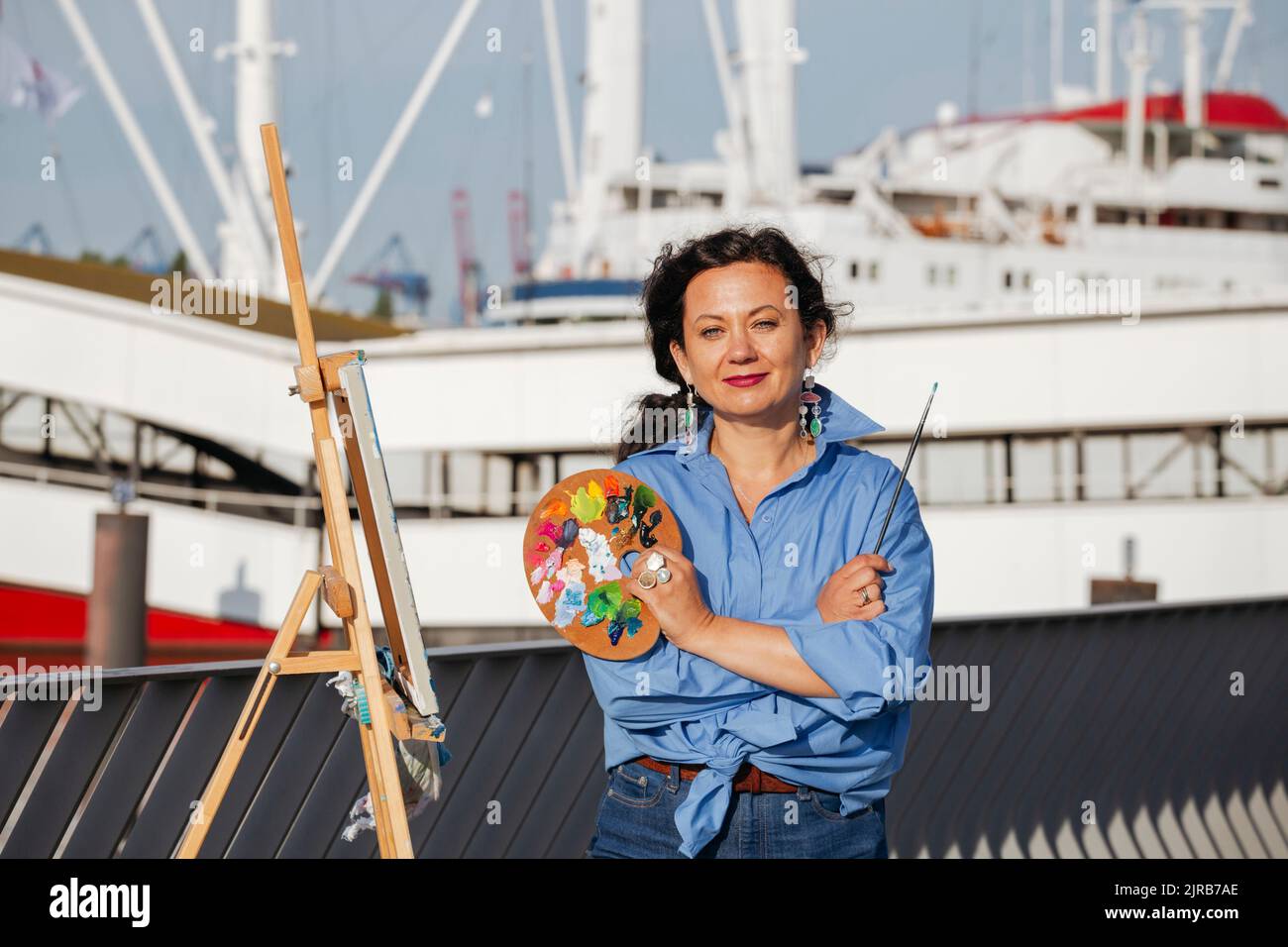 Smiling confident painter holding palette standing by easel Stock Photo ...