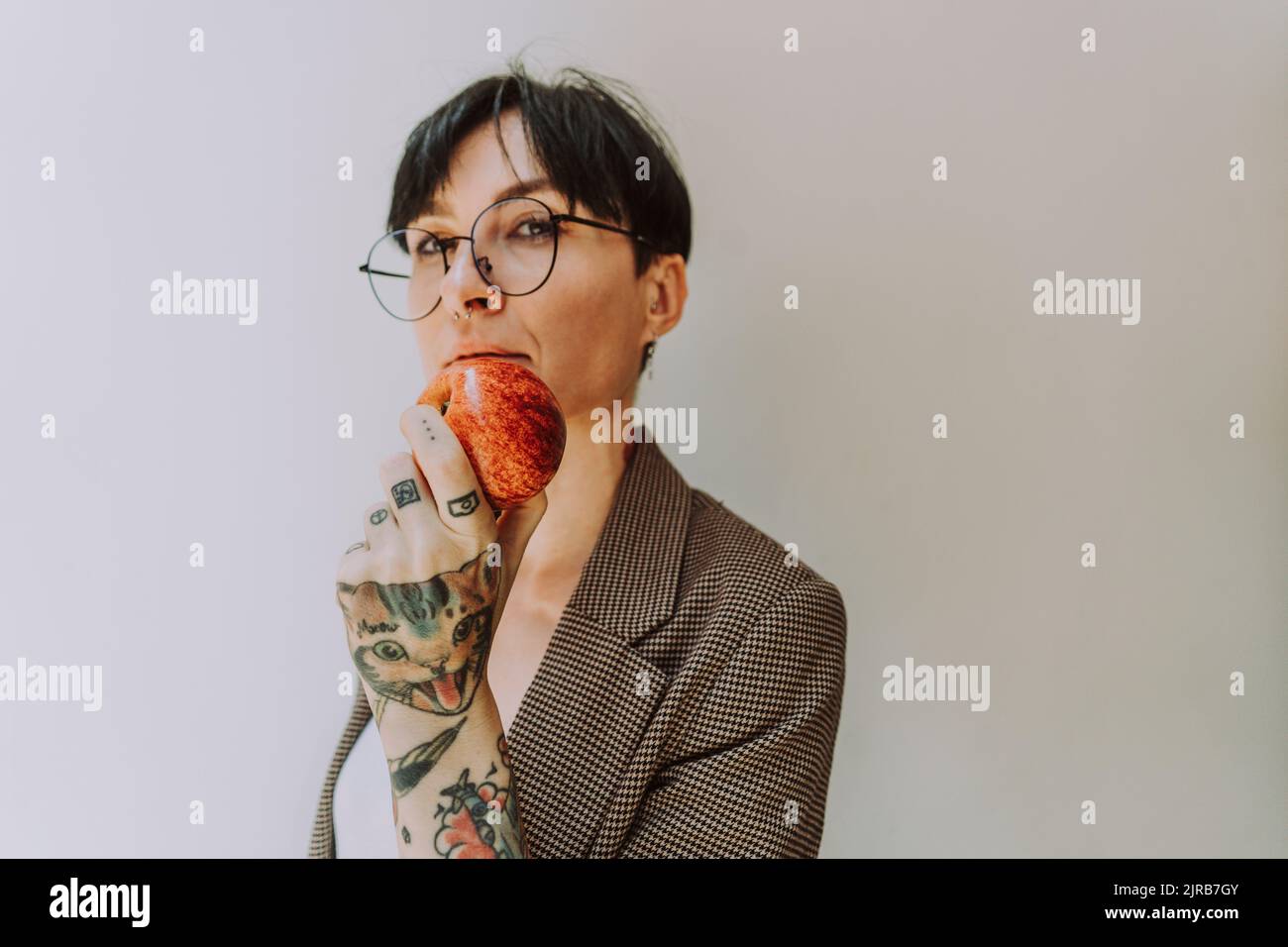 Businesswoman eating apple standing in front of wall Stock Photo - Alamy