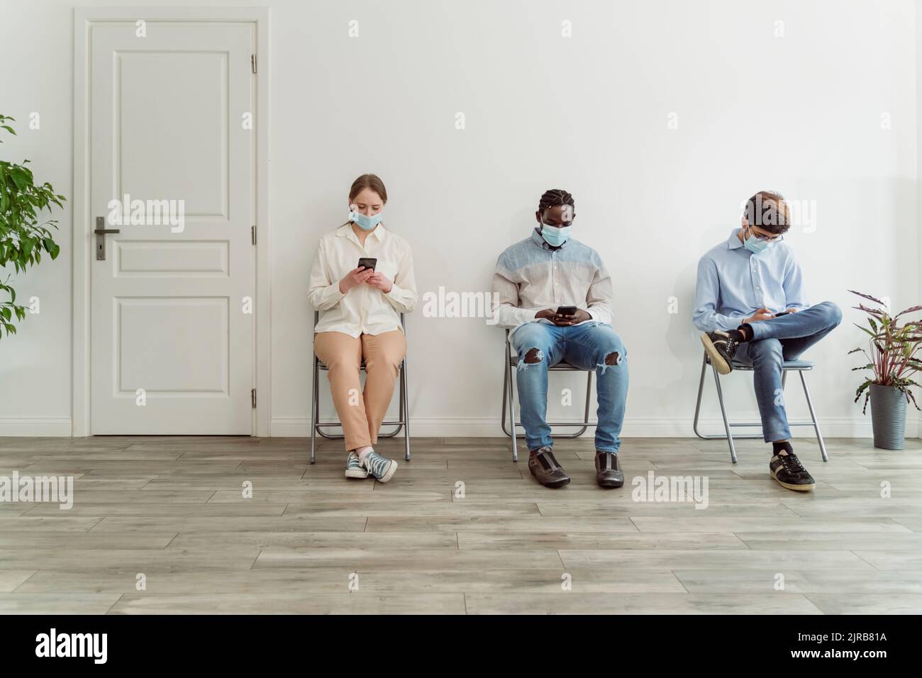 People wearing face masks sitting on chairs in waiting area Stock Photo ...