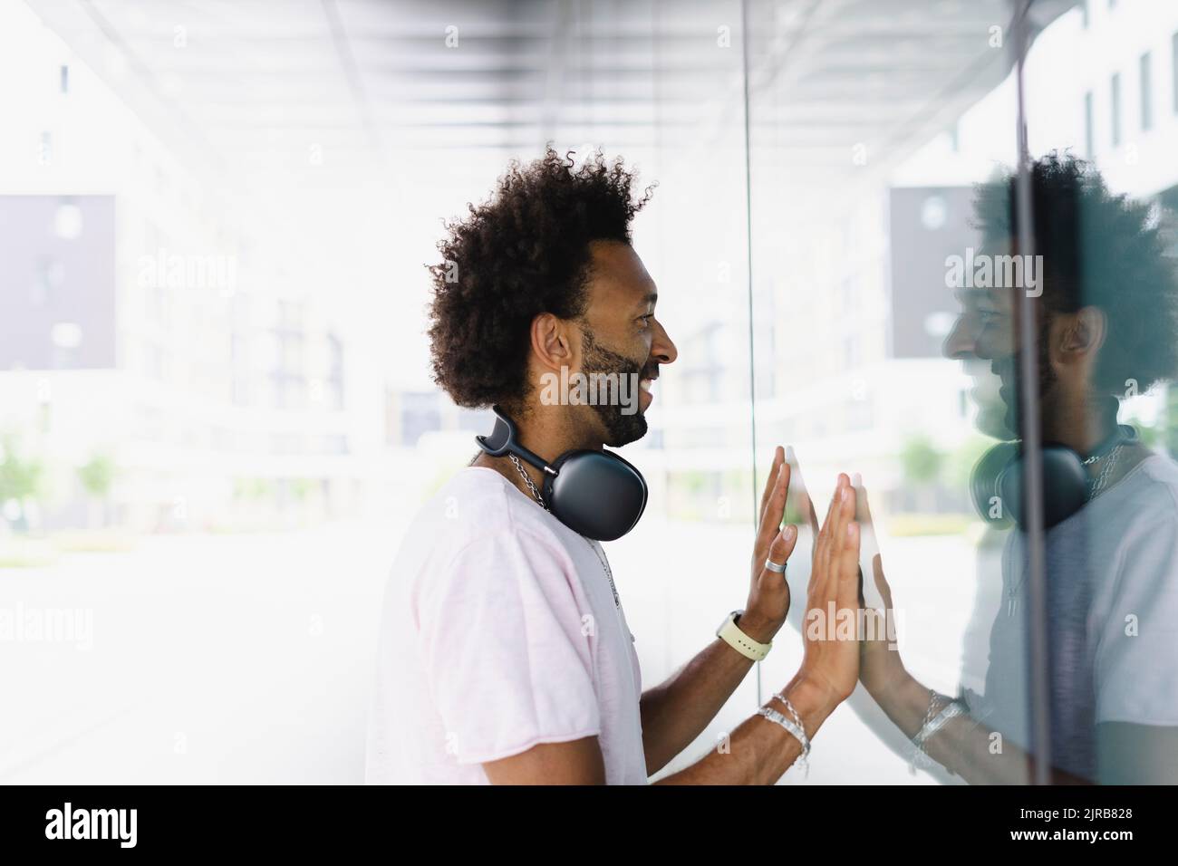 Smiling man touching reflection on glass wall Stock Photo - Alamy