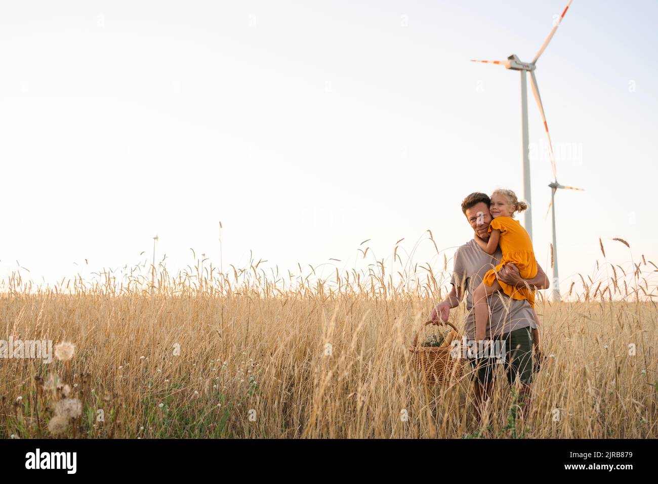 Father carrying daughter at wheat field with wind turbines Stock Photo ...