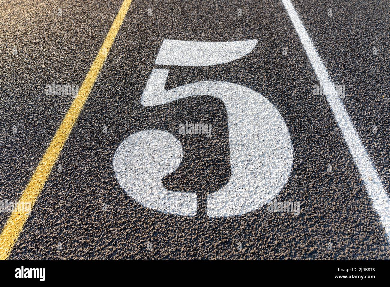 Close up lane number five, 5, on a new black running track with white ...